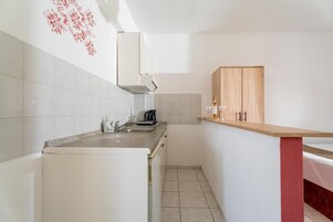 Cozinha compacta com armários brancos, bancada de madeira e parede com detalhe em vermelho.