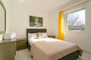 Quarto com cama, mesa de cabeceira, janela com cortinas e um quadro na parede.