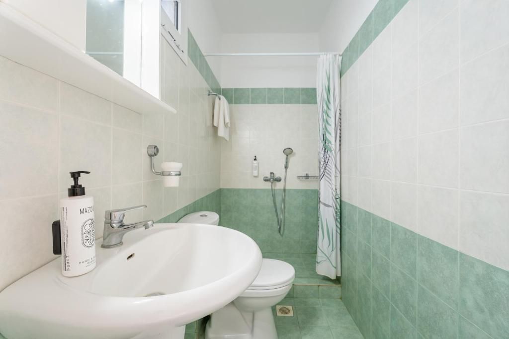 Casa de banho com lavatório branco, sanita e chuveiro com parede revestida a mosaico verde e branco.