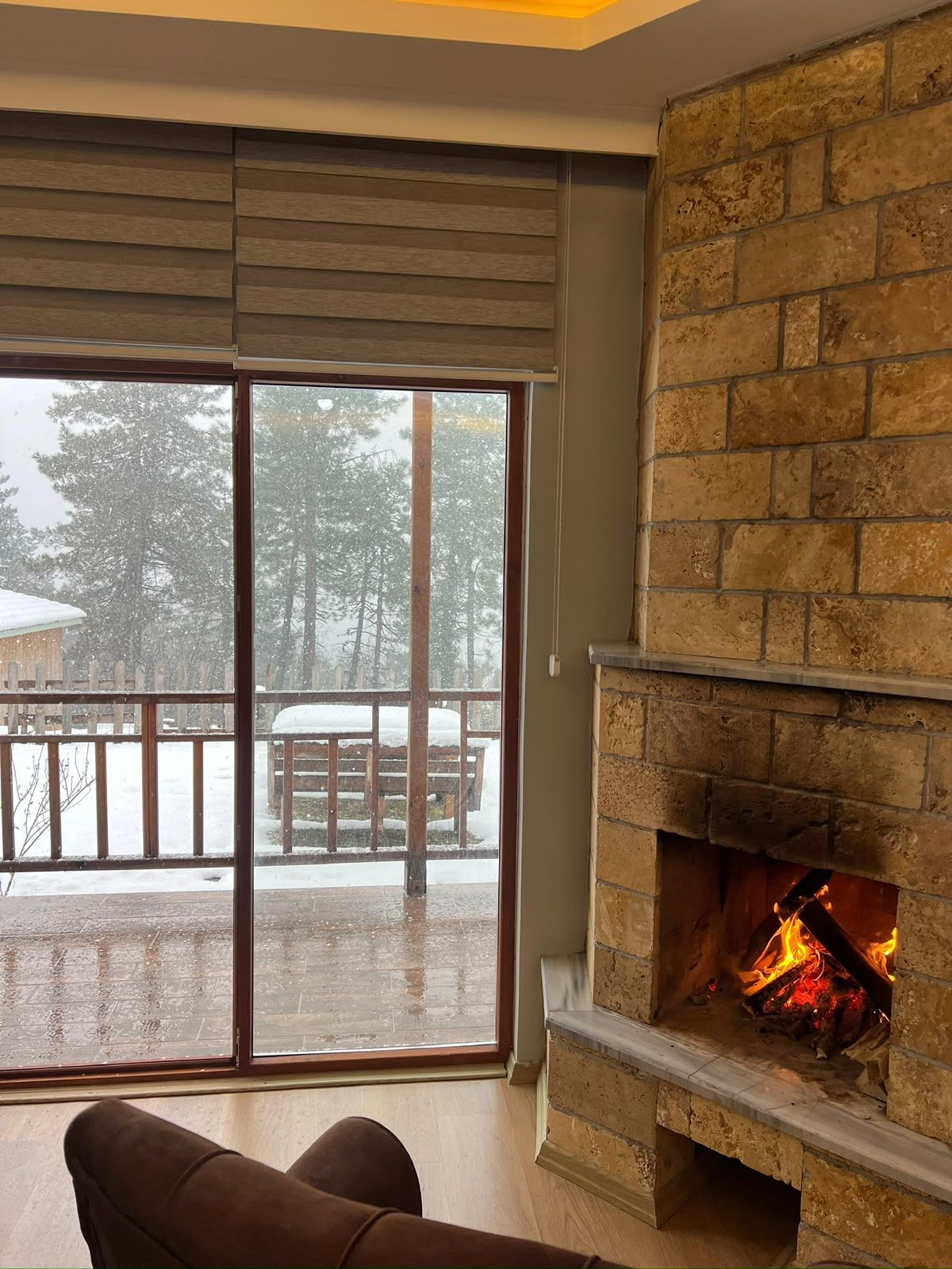 Quarto com lareira, porta de vidro deslizante para um deck coberto de neve e sofá marrom.
