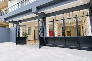 Uma fachada moderna de edifício com portão de metal, piso xadrez e varanda.