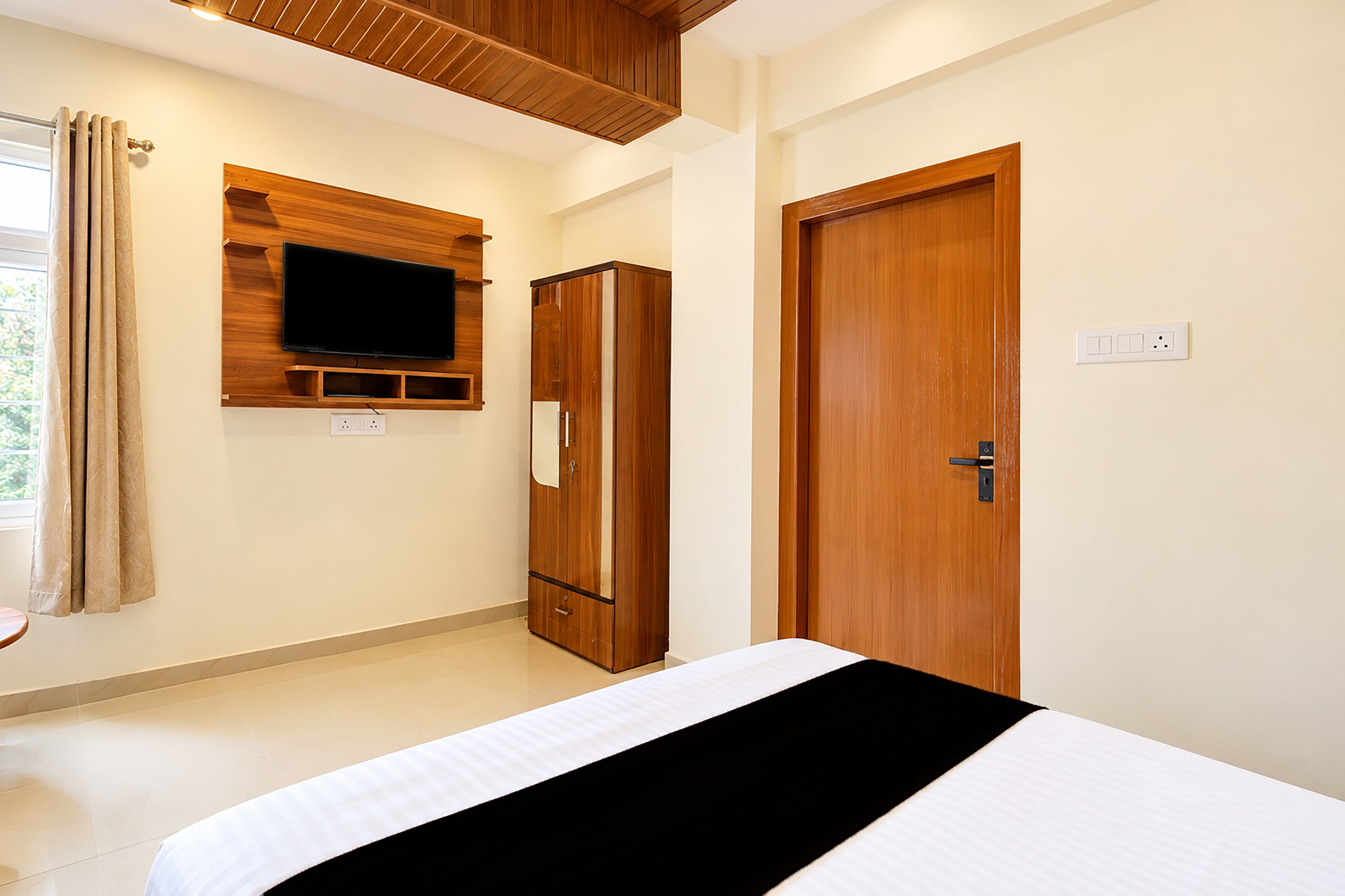 Quarto com cama, guarda-roupa, televisão na parede e porta.