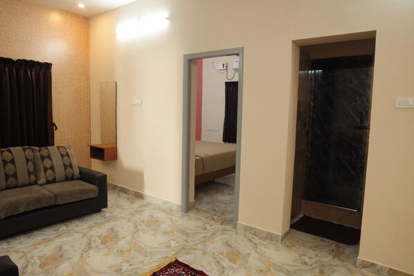 Sala de estar com sofá, tapete estampado e corredor que dá para um quarto com cama.