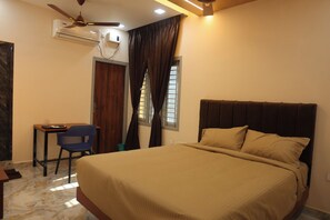 Quarto com cama, escrivaninha, cadeira, ar condicionado e ventoinha no teto.
