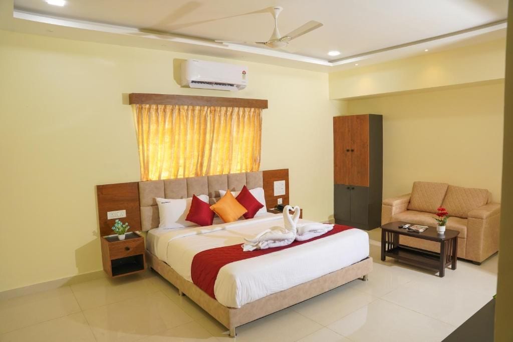 Quarto de hotel com cama, mesa de cabeceira, sofá, mesa de centro, ar condicionado e ventoinha no teto.