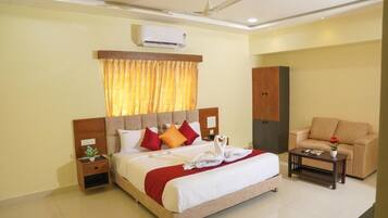 Quarto de hotel com cama, mesa de cabeceira, sofá, mesa de centro, ar condicionado e ventoinha no teto.