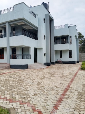 Um edifício moderno de vários andares com telhado plano, varandas e um pátio pavimentado.