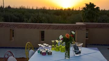 Mesa posta ao ar livre com diversos copos e um vaso de flores, com vista para uma paisagem natural.