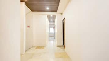 Um corredor com piso ladrilhado, paredes brancas e teto com iluminação embutida.