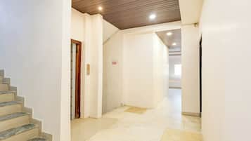 Interior limpo e moderno, com uma escada que leva a um patamar, sinal de saída de incêndio e um corredor com piso ladrilhado.
