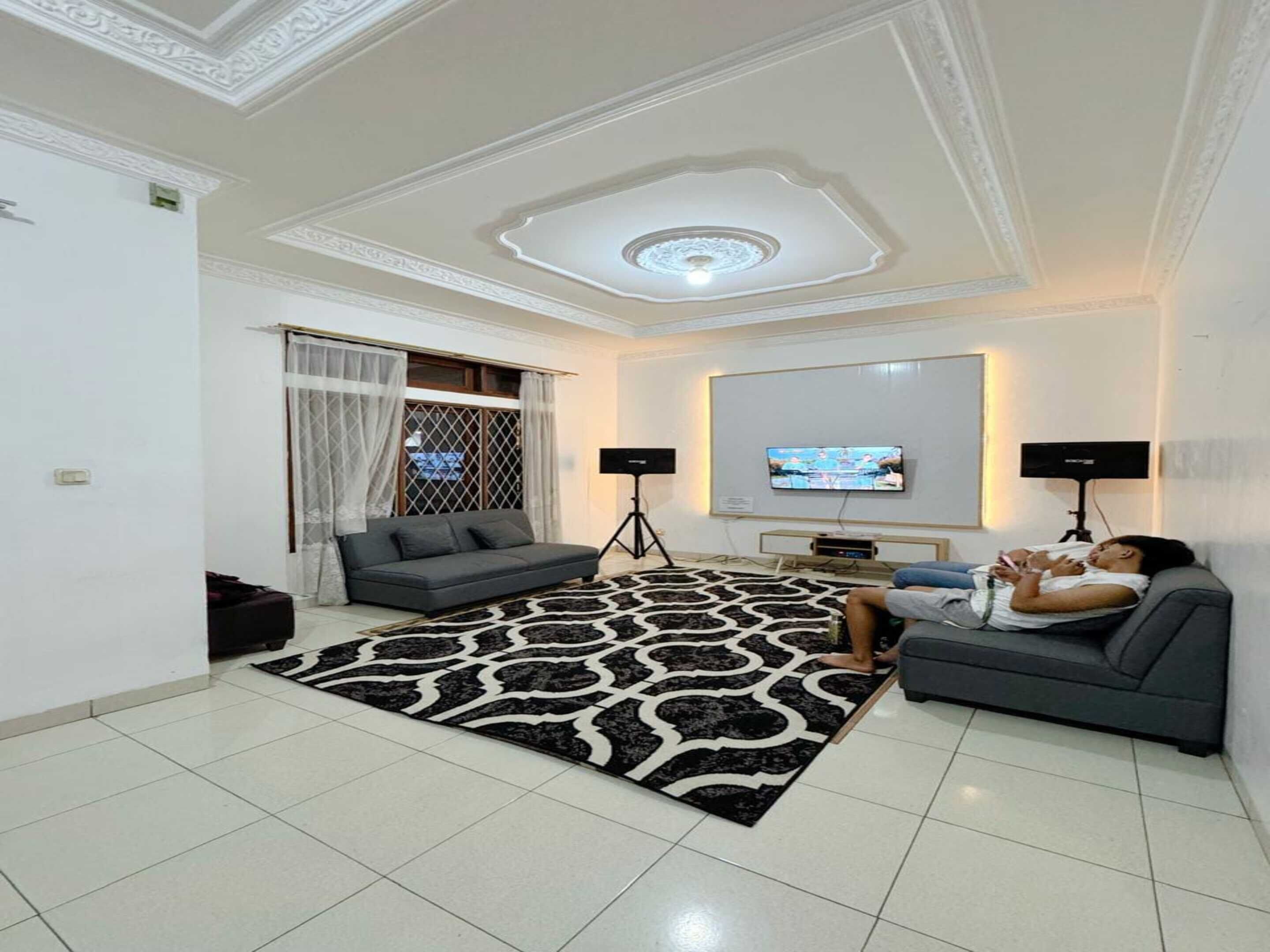 Sala de estar com sofá, televisão, tapete estampado e teto com molduras decorativas.