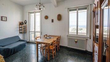Um quarto com mesa de jantar de madeira, cadeiras, sofá azul, radiador e janela com vista.