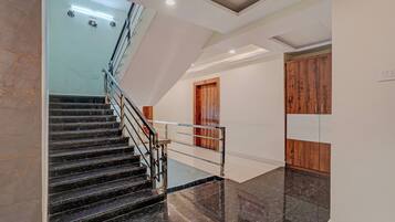 Uma escada com corrimão de metal leva a um patamar, uma porta de madeira e uma parede com interruptor de luz.