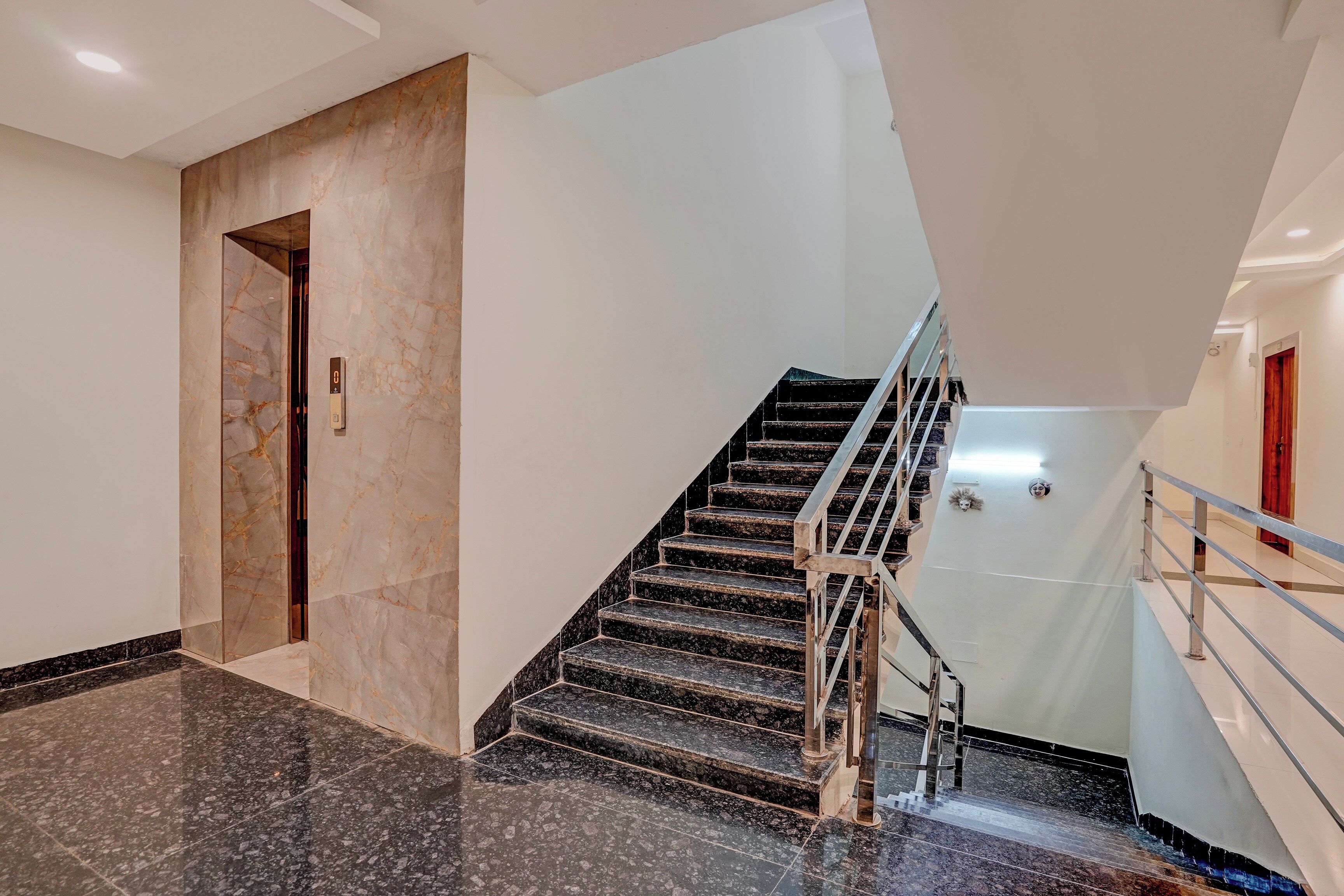 Interior moderno com parede de mármore, escada com corrimão de metal e painel digital de elevador.