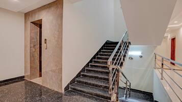 Interior moderno com parede de mármore, escada com corrimão de metal e painel digital de elevador.
