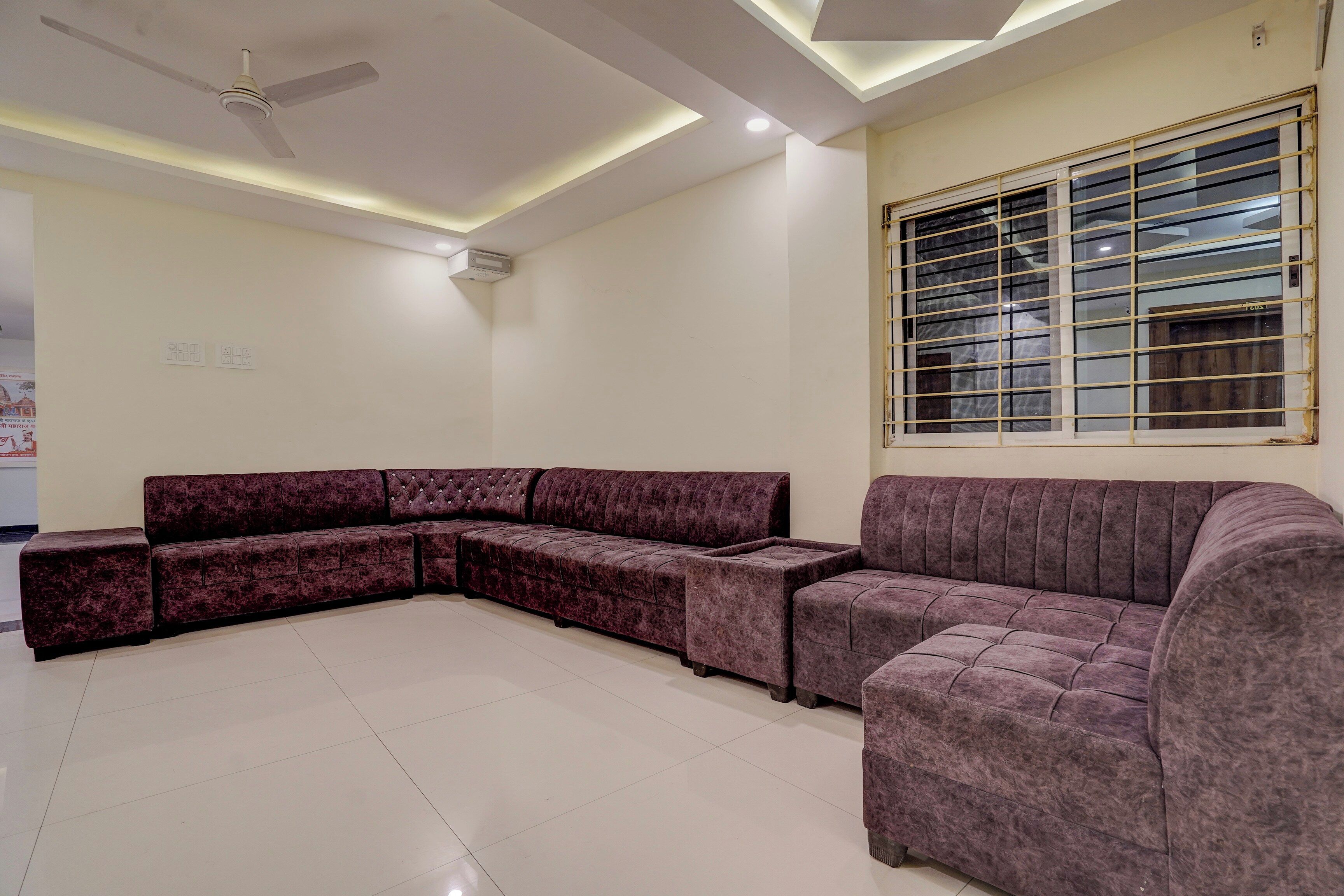 Sala de estar com sofá seccional, ventilador de teto, iluminação embutida e janela com grades.