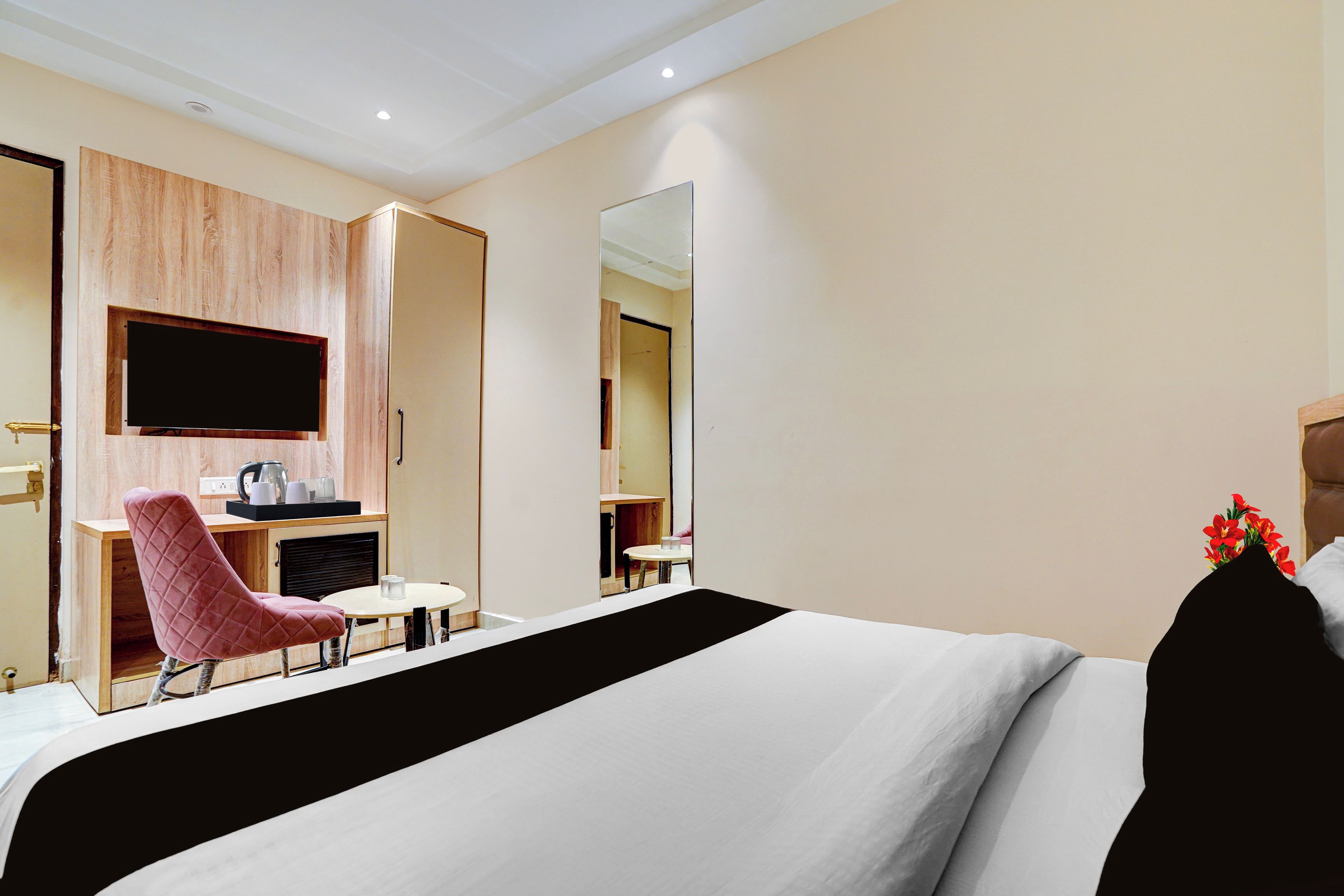 Quarto de hotel com cama, televisão na parede, cadeira, mesinha e espelho.