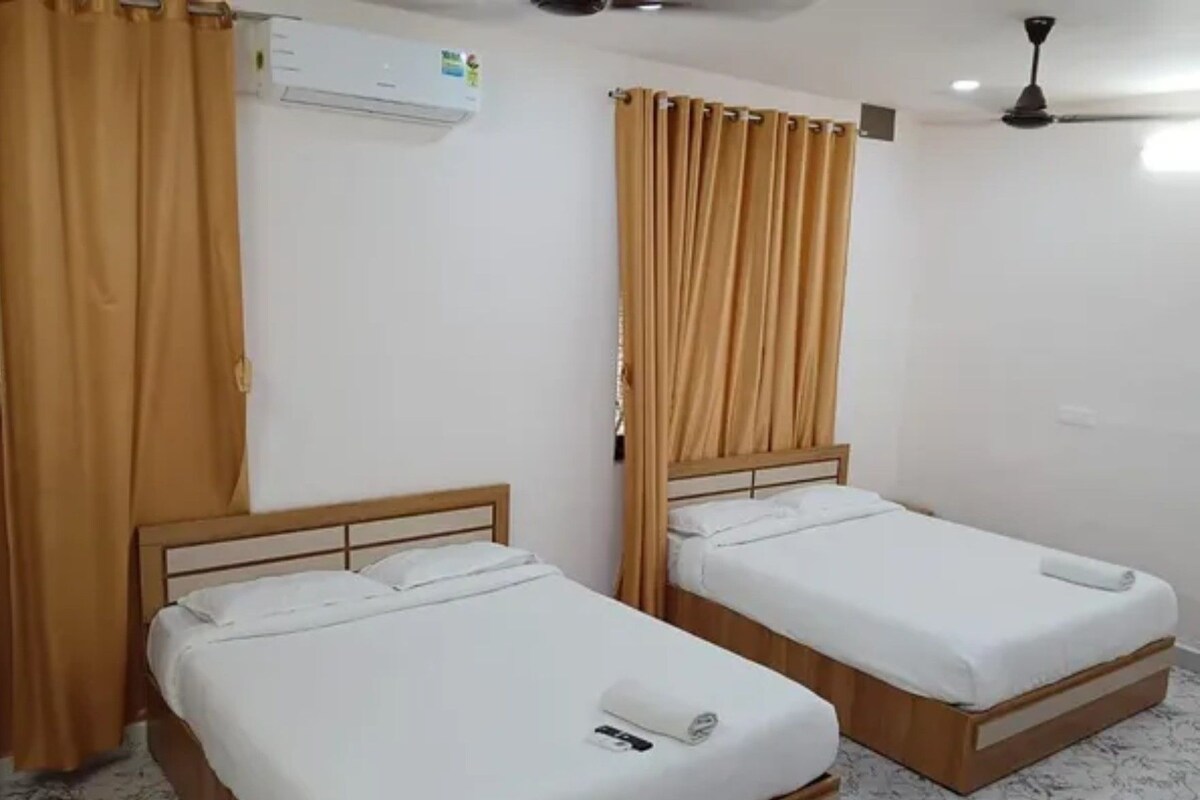 Quarto de hotel com duas camas de solteiro, ventilador de teto, aparelho de ar condicionado e piso com padrão marmorizado.