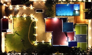Vista aérea de um hotel com piscina, quadra de tênis e jardins bem cuidados.