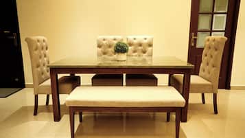Uma sala de jantar com uma mesa retangular, quatro cadeiras estofadas, um banco e um vaso de planta.