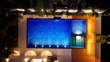 Piscina retangular com revestimento em azulejo, rodeada por um deck de madeira e uma parede com jardim vertical.