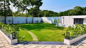 Um jardim bem cuidado com um caminho pavimentado, cercado por um muro branco e diversas plantas.