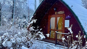 Uma cabana de madeira com telhado coberto de neve e um banco em frente.