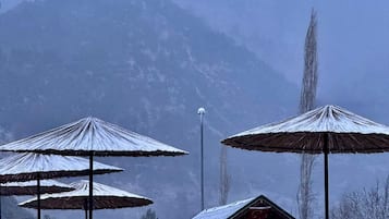 Uma área externa coberta de neve com guarda-sóis, uma estrutura de madeira e montanhas ao fundo.