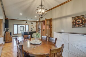 Uma sala de jantar com uma mesa de madeira, cadeiras, um lustre e vista para a cozinha.