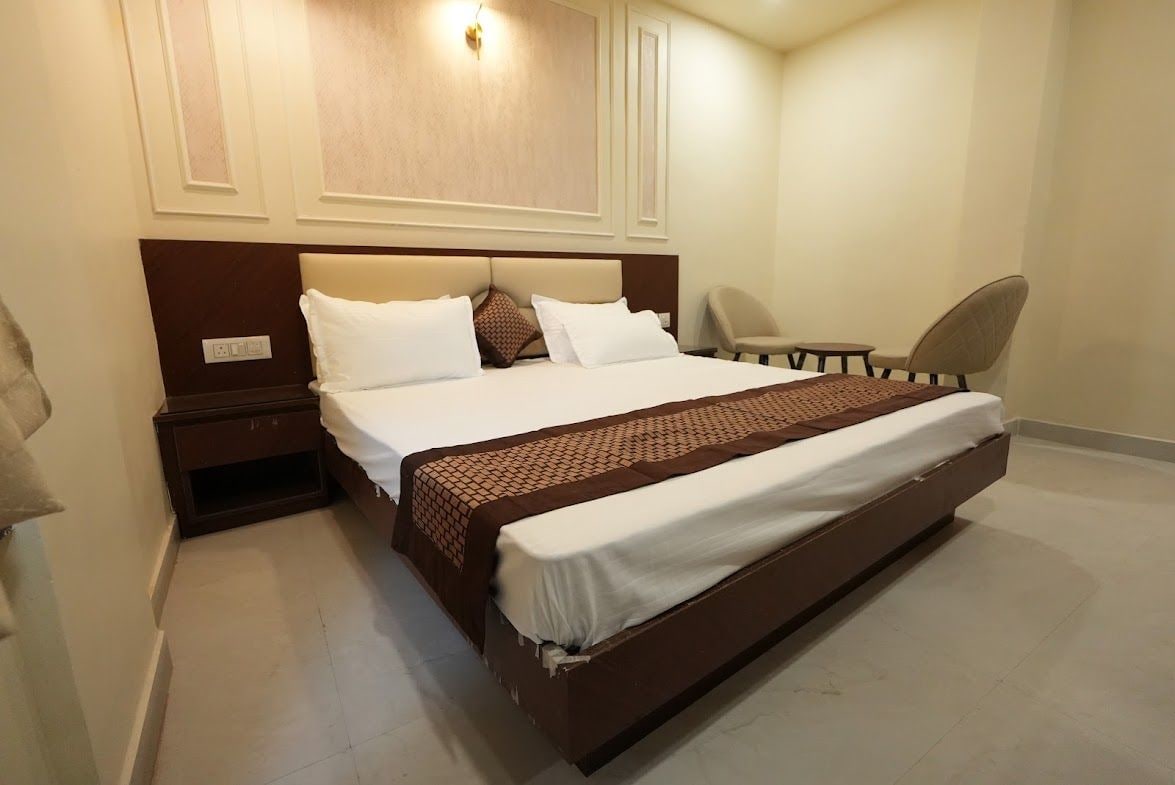 Quarto de hotel com uma cama grande, mesa de cabeceira, uma cadeira e luminária na parede.