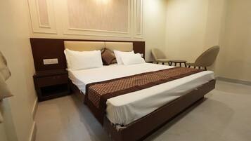 Quarto de hotel com uma cama grande, mesa de cabeceira, uma cadeira e luminária na parede.