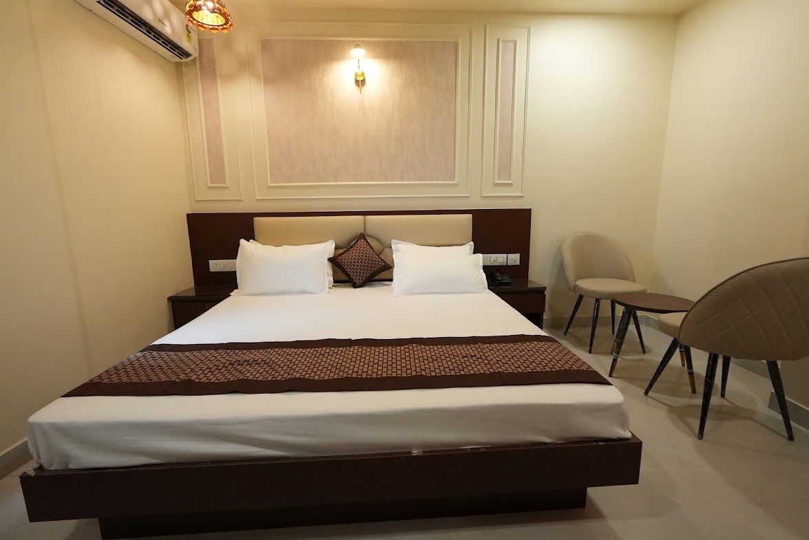 Quarto de hotel com uma cama grande, uma mesinha de cabeceira, uma cadeira e luminária na parede.