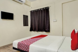 Quarto de hotel com cama, televisão de tela plana na parede, janela com cortinas escuras e tomada.