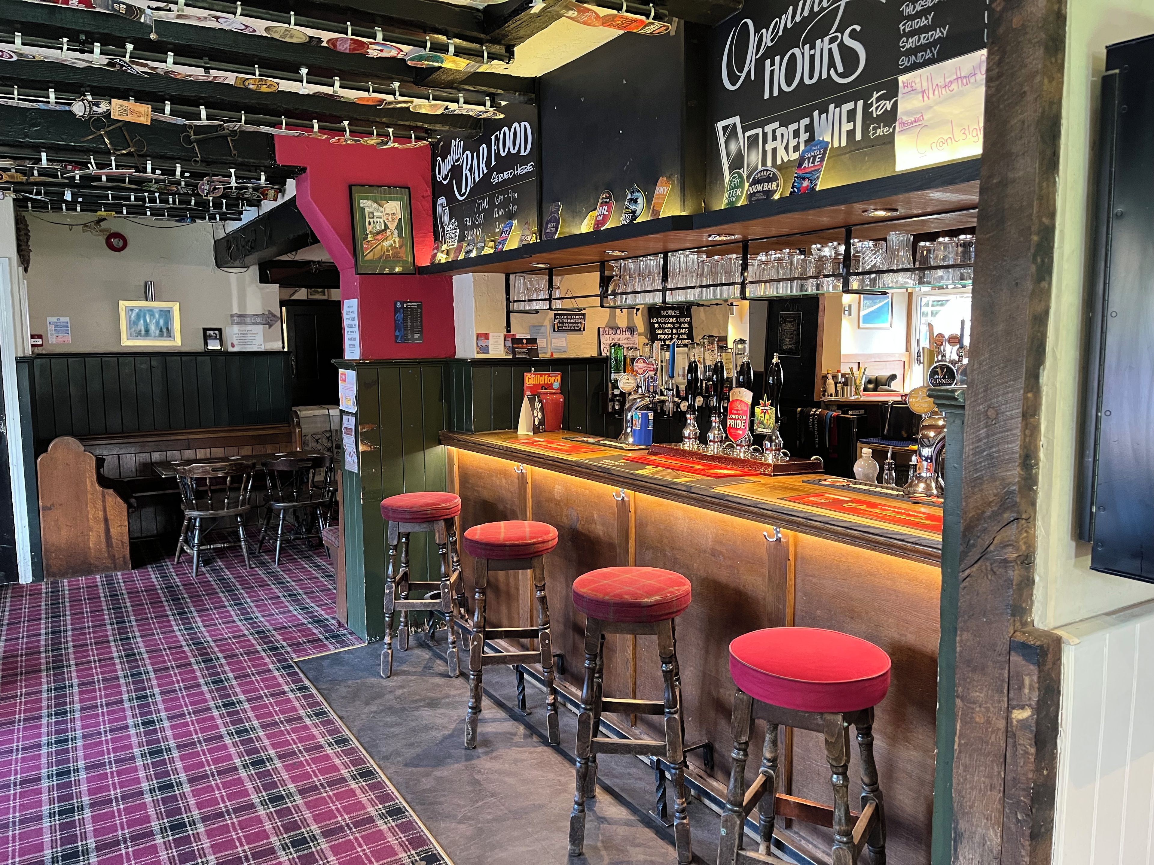 Uma área de bar com banquetas, balcão e diversas garrafas e copos.