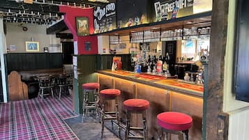 Uma área de bar com banquetas, balcão e diversas garrafas e copos.