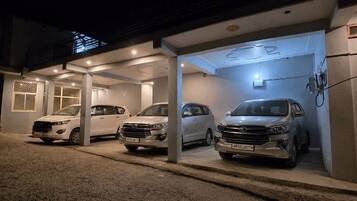 Área de estacionamento coberta com três carros estacionados sob uma estrutura com claraboia.