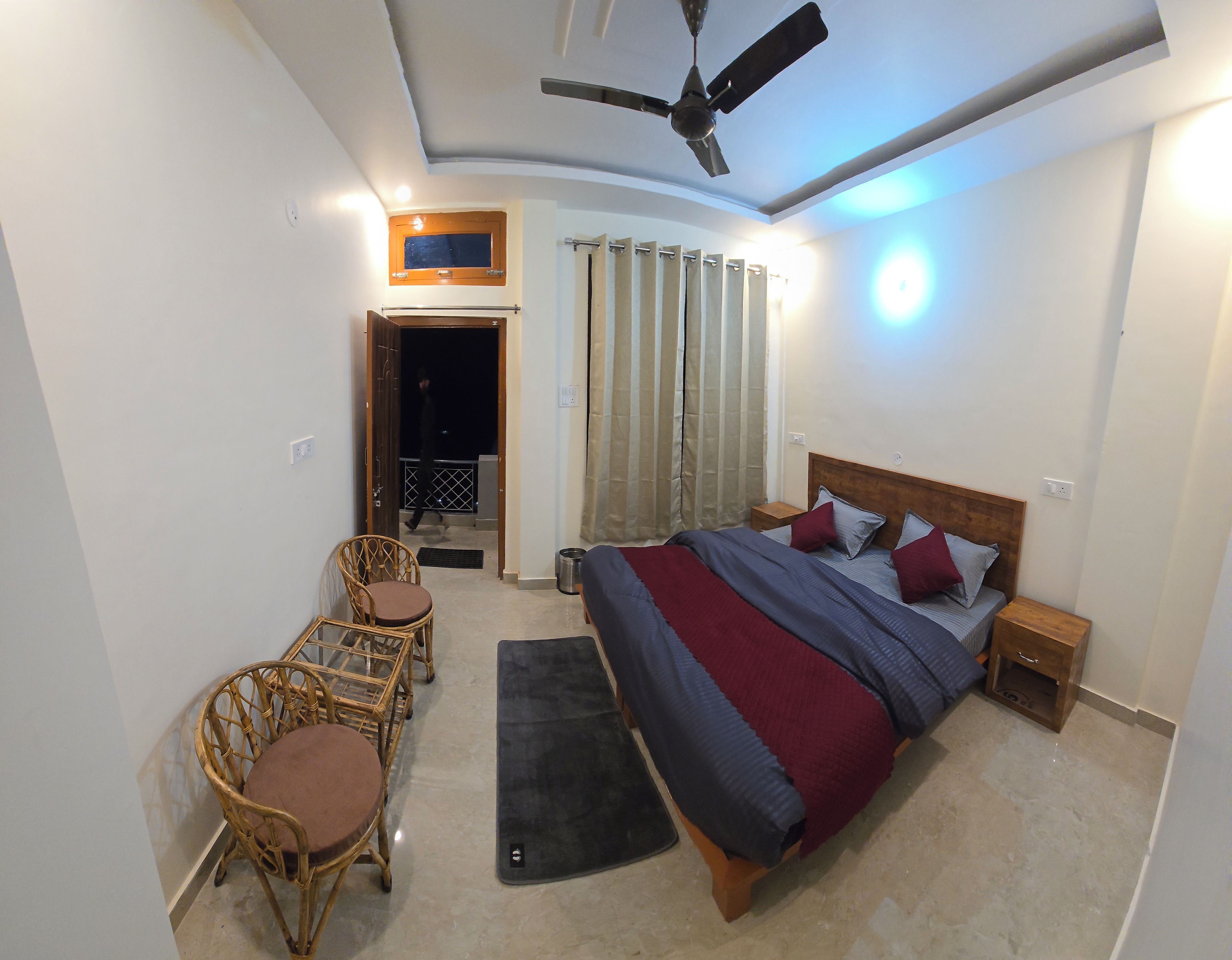 Quarto com cama, mesas de cabeceira, ventilador de teto e porta que dá para uma varanda.