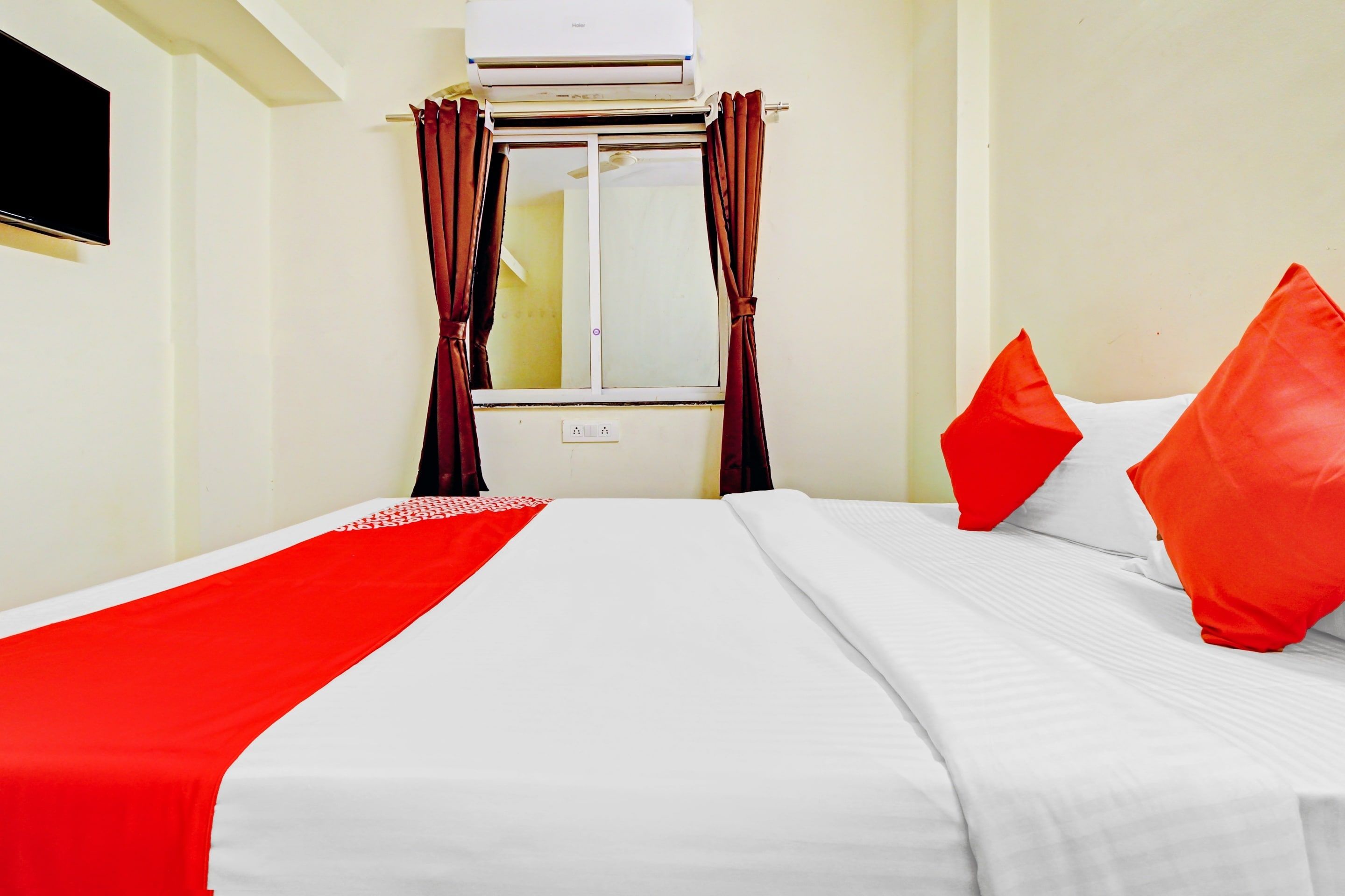 Quarto de hotel com cama, janela com cortinas, ar-condicionado e televisão de tela plana fixada na parede.