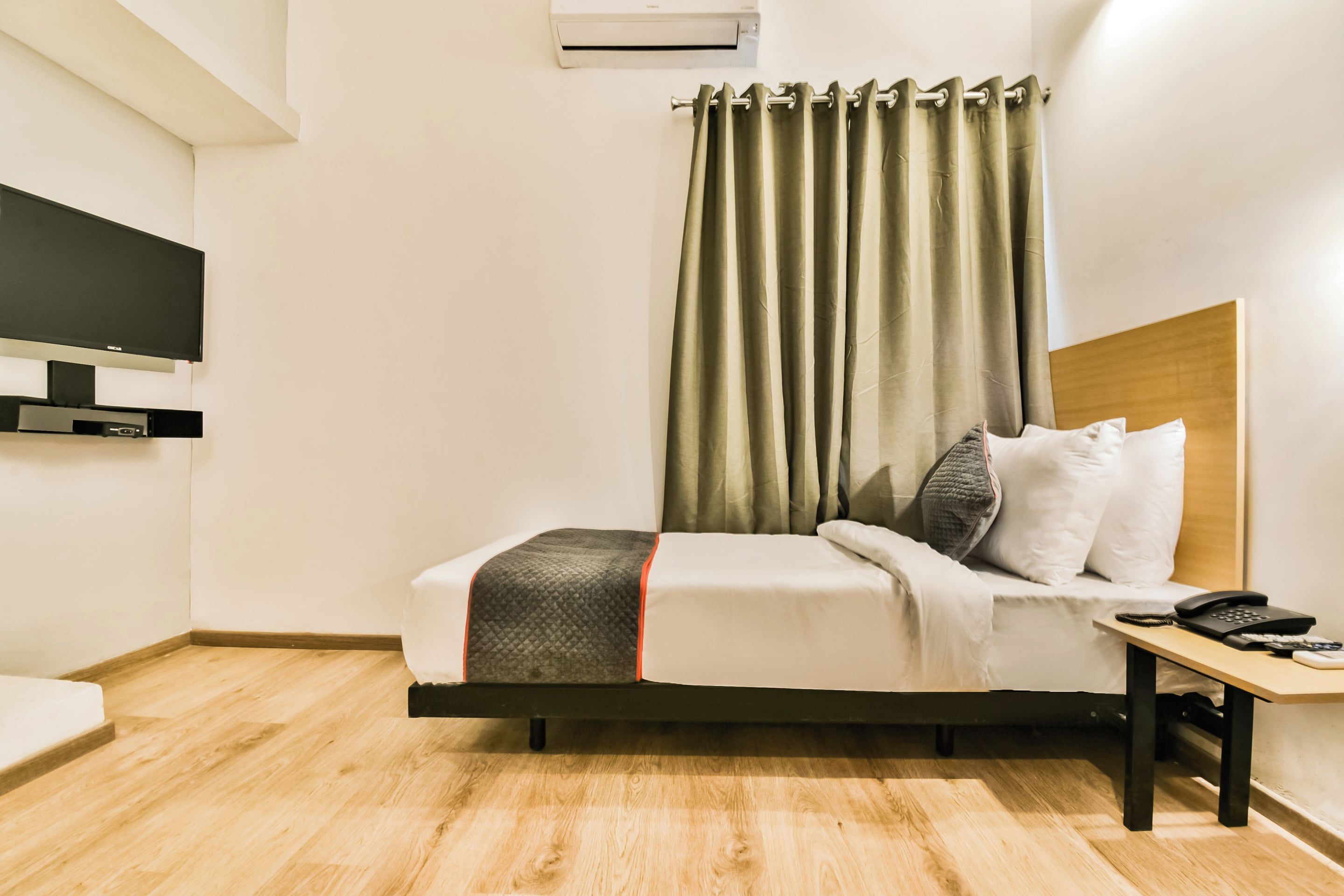 Quarto de hotel com uma cama, televisão, escrivaninha e um cortinado.