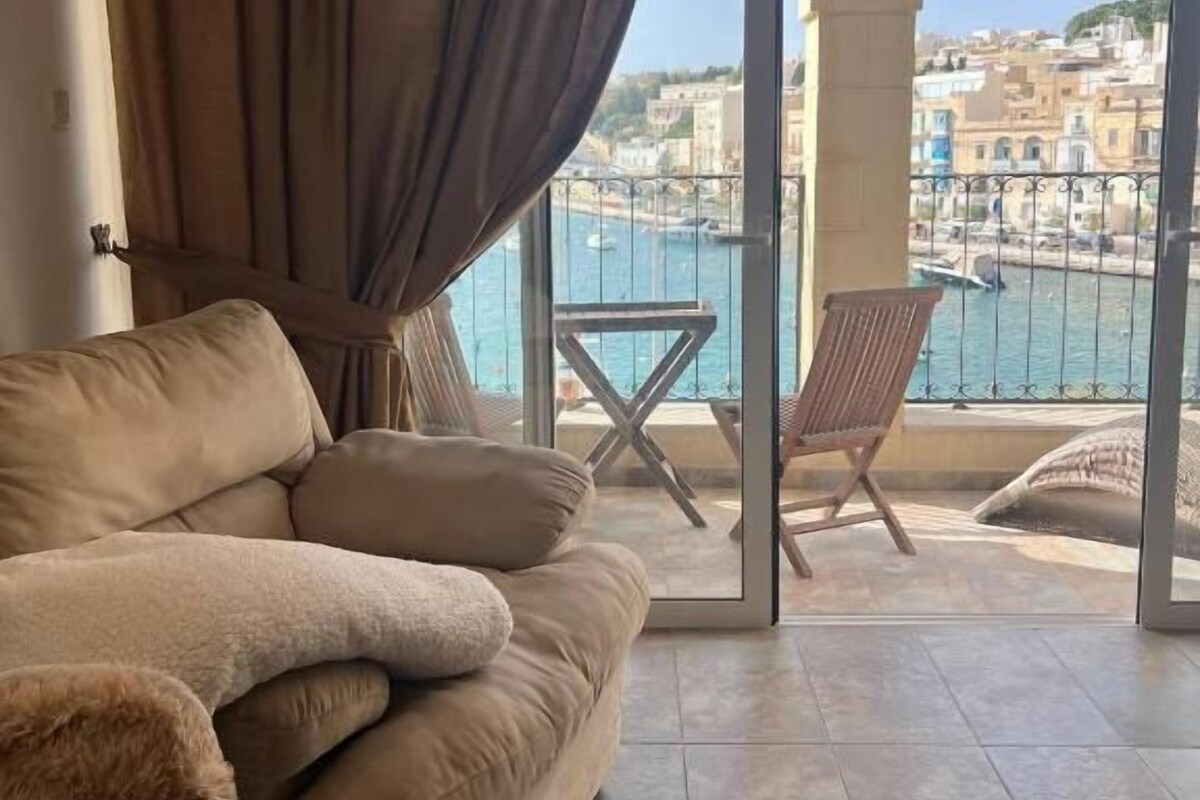 Quarto com sofá, poltrona e vista para a água e edifícios.