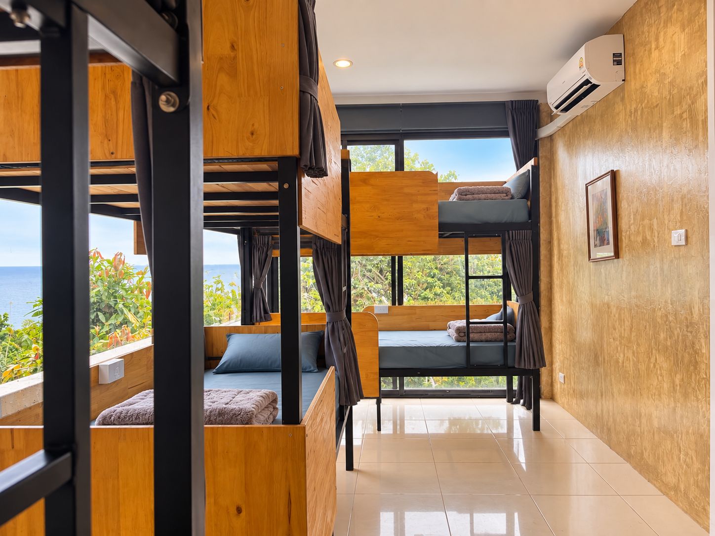 Quarto com beliche e vista para o mar, paredes de madeira e janela com cortinas.
