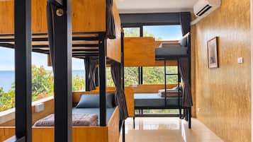 Quarto com beliche e vista para o mar, paredes de madeira e janela com cortinas.