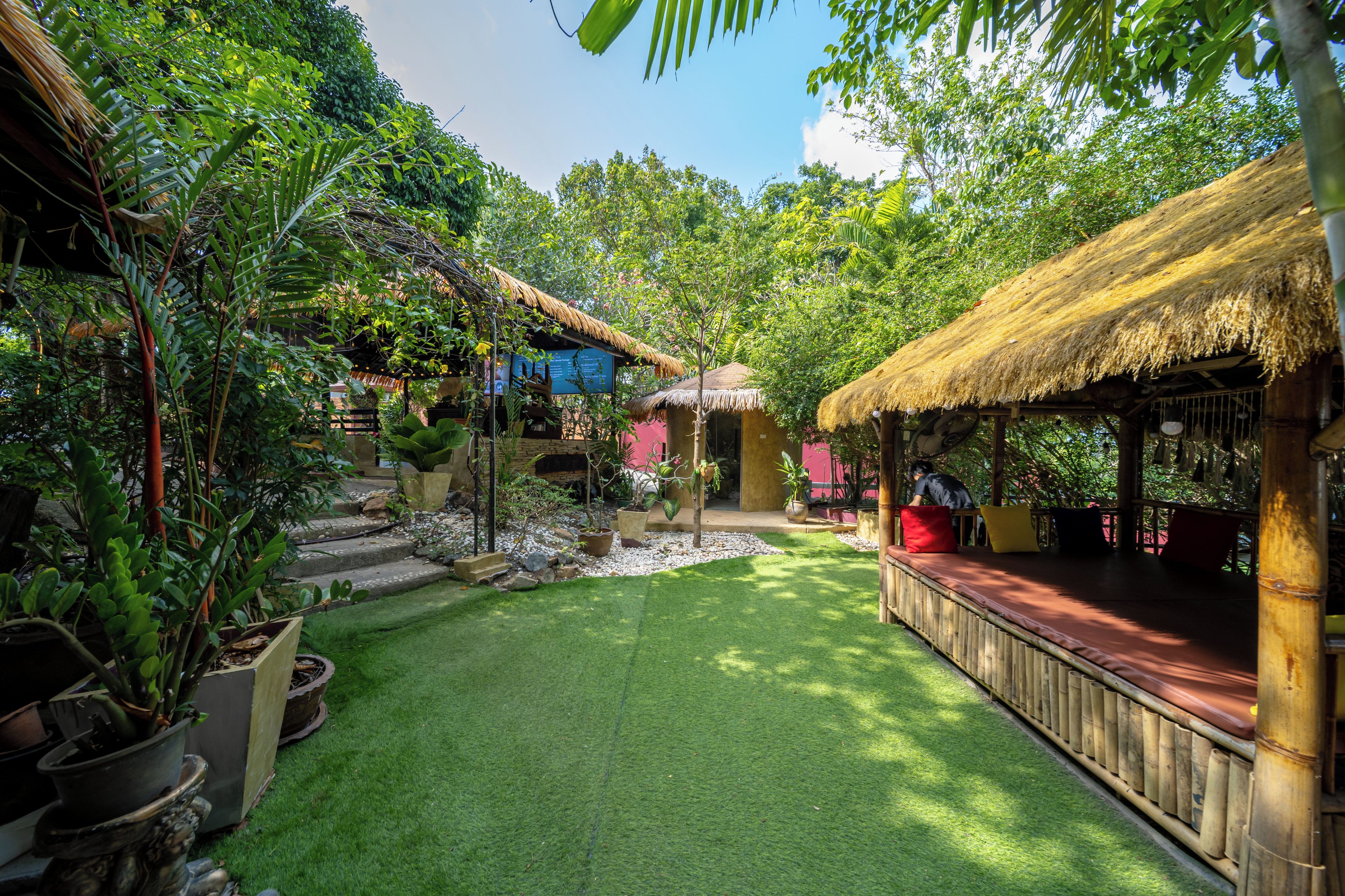 Um jardim exuberante com uma construção de colmo, vasos de plantas e um gramado bem cuidado.