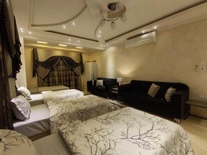 Quarto de hotel com uma cama grande, duas camas menores, um sofá preto, uma TV e um aparelho de ar condicionado.