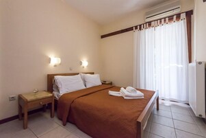 Quarto de hotel com cama, mesas de cabeceira, ar condicionado e janela com cortinas.