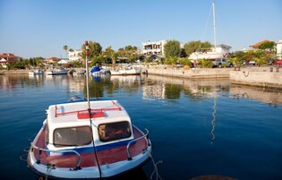 Marina com barcos atracados, água calma e edifícios ao fundo.