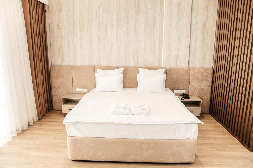 Quarto de hotel com uma cama grande, duas mesas de cabeceira e uma cabeceira de madeira.