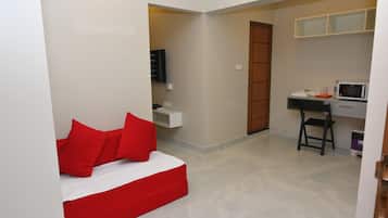 Quarto compacto com cama, escrivaninha, cadeira, televisão e micro-ondas.