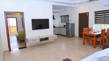 Uma sala de estar moderna com televisão de tela plana, uma área de jantar com mesa e cadeiras, e uma cozinha com geladeira e micro-ondas.