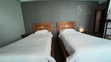 Quarto duplo com duas camas de solteiro, cabeceiras de madeira, mesa de cabeceira com abajur e espelho na parede.